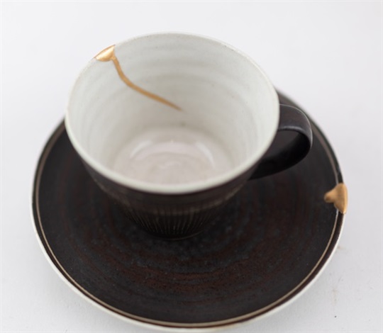 a stoneware cup and saucer partially covered in manganese glaze with ...